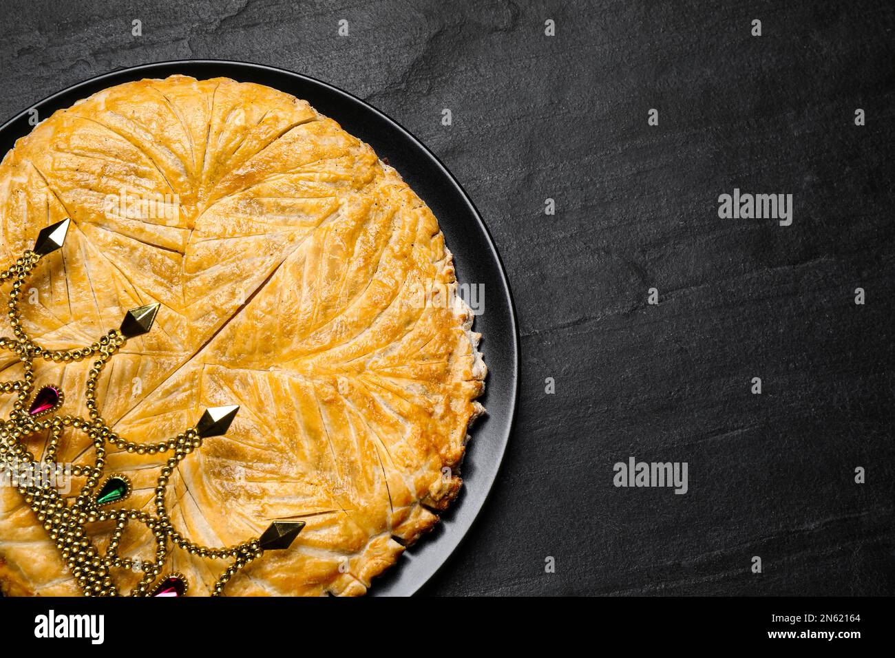 Traditional galette des rois with crown on black table, top view. Space ...
