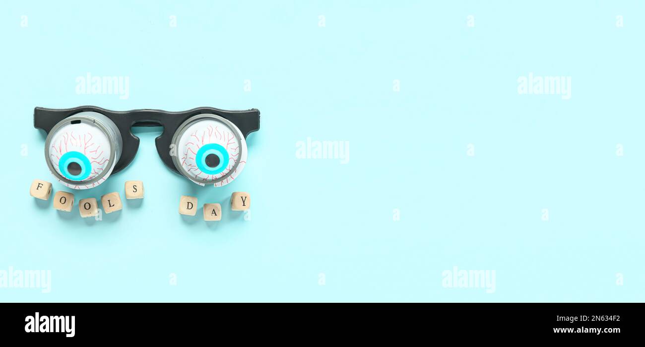 Funny glasses and text FOOLS DAY on light blue background with space ...