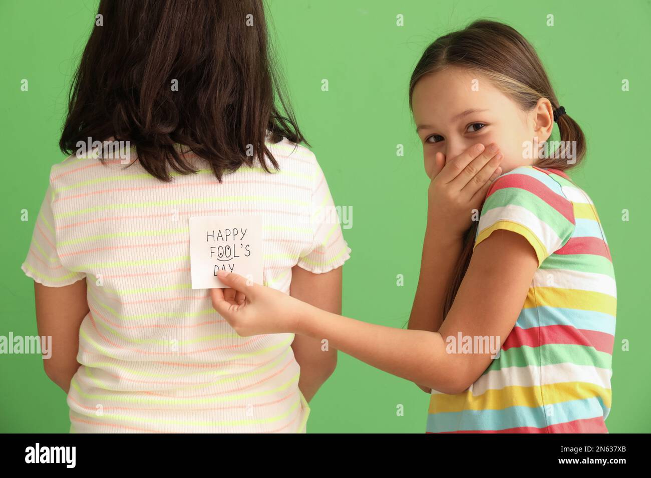 Little girl playing a prank on her sister against green background ...