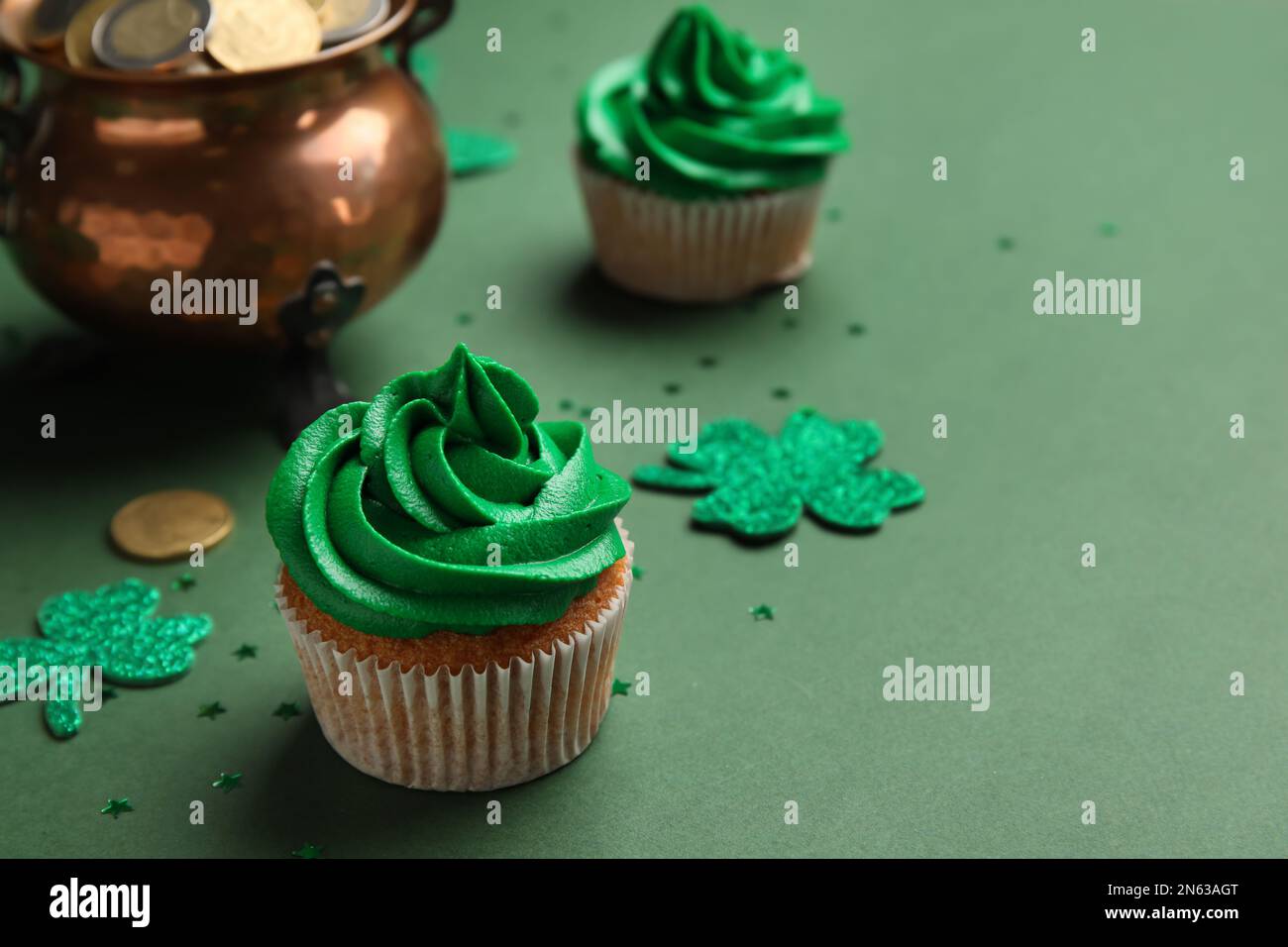 Tasty cupcakes for St. Patrick's Day, clovers and pot of coins on green ...