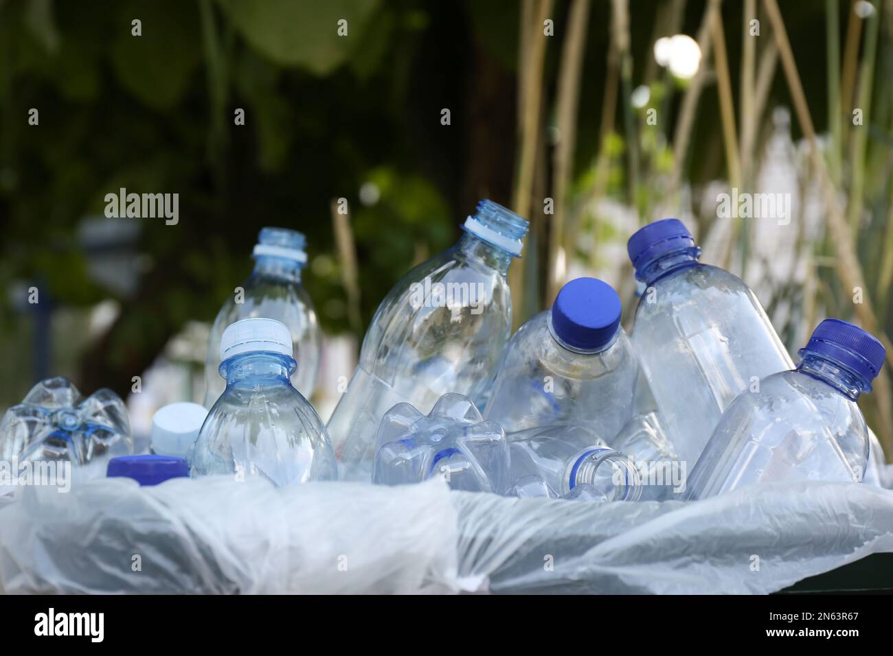 Many used plastic bottles in trash bin outdoors, closeup. Recycling ...