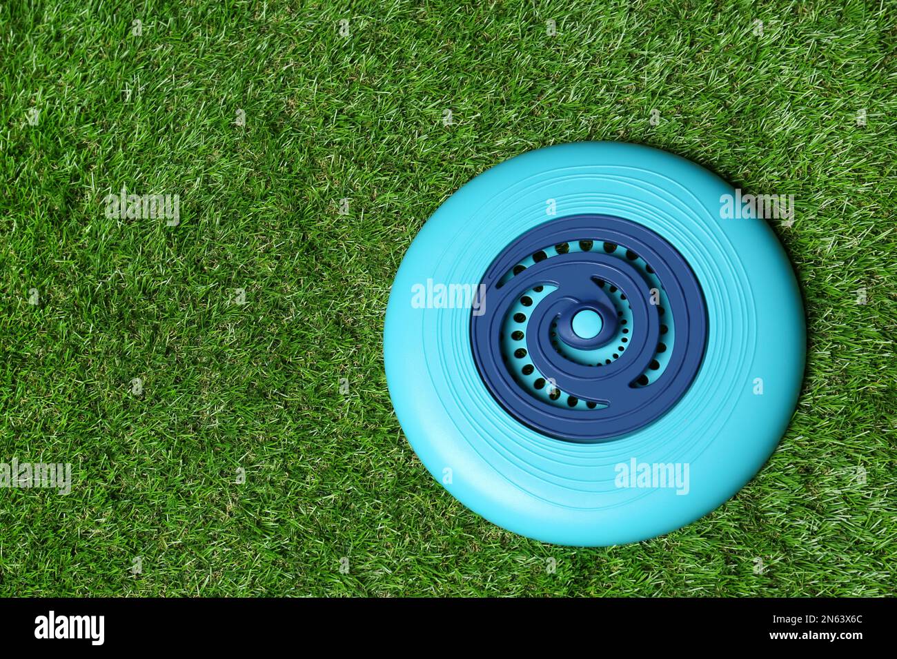 Light blue plastic frisbee disk on green grass, top view. Space for ...