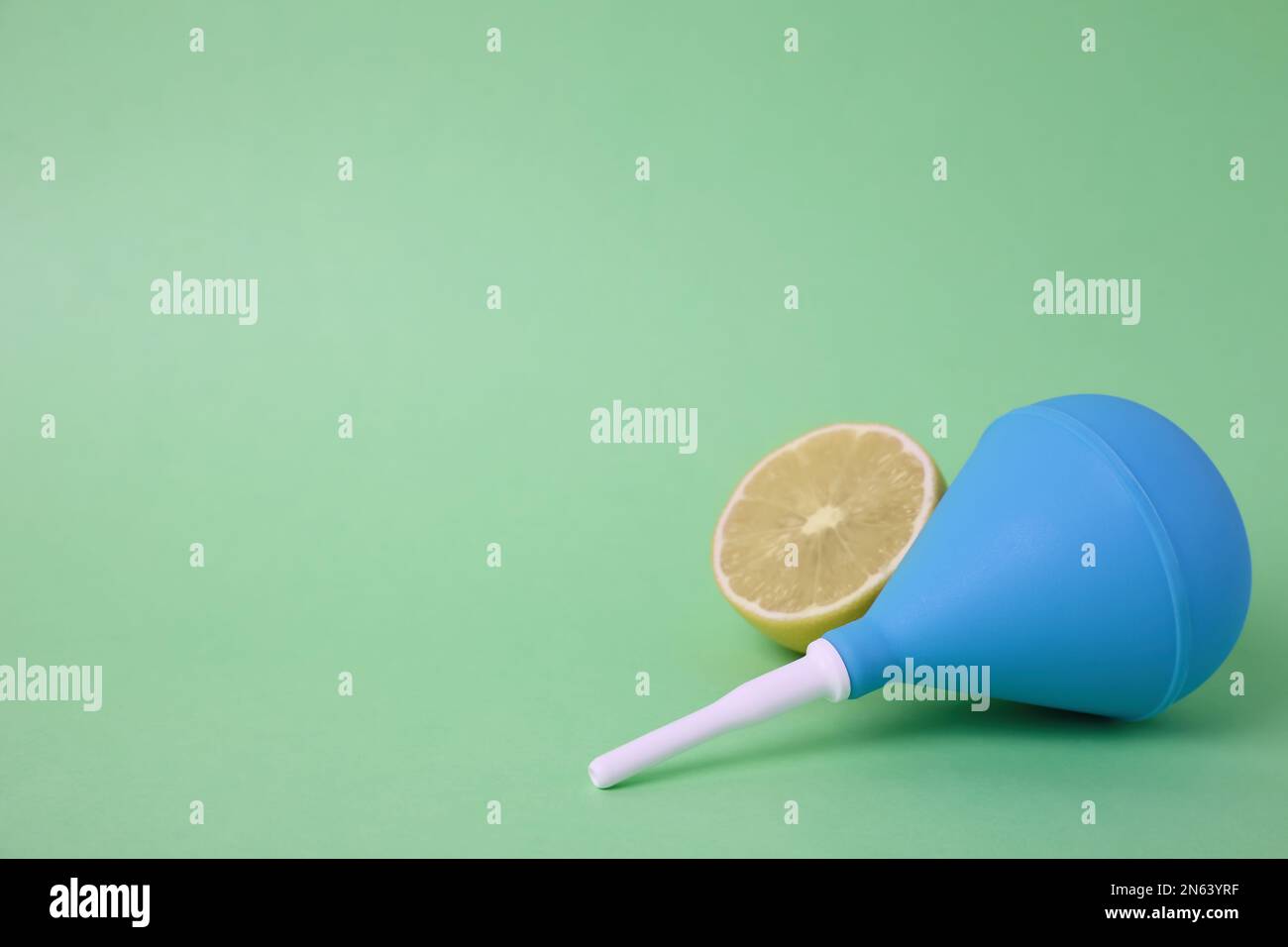 Enema and half of lemon on green background, space for text. Medical ...