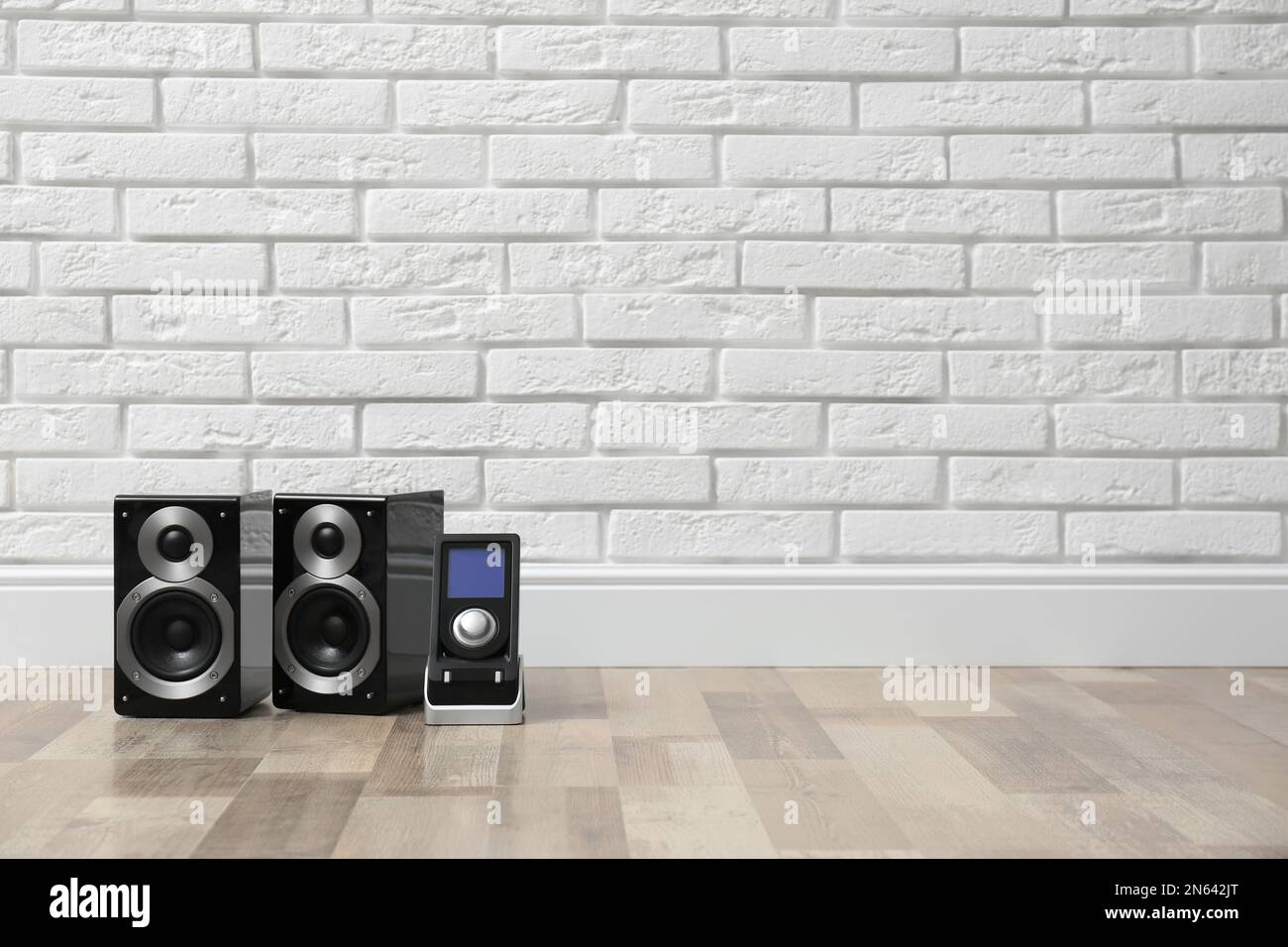 Modern powerful audio speakers and remote on floor near white brick ...