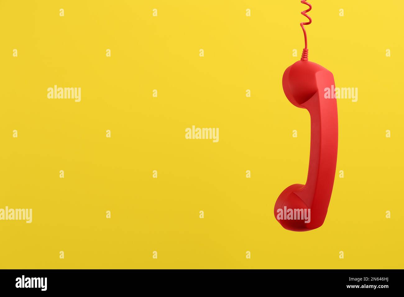 Red corded telephone handset hanging on yellow background, space for ...