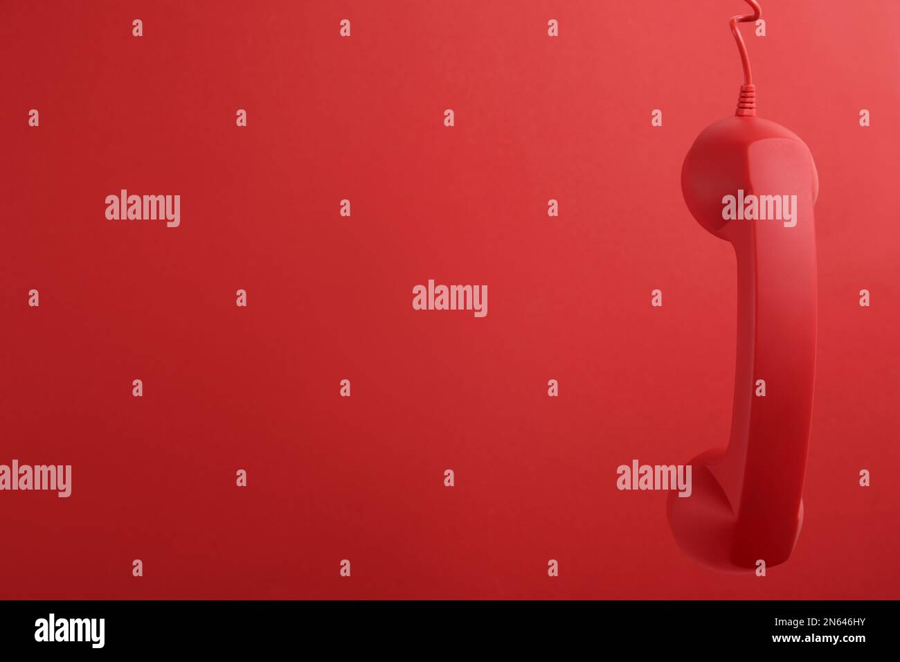 Corded telephone handset hanging on red background, space for text ...