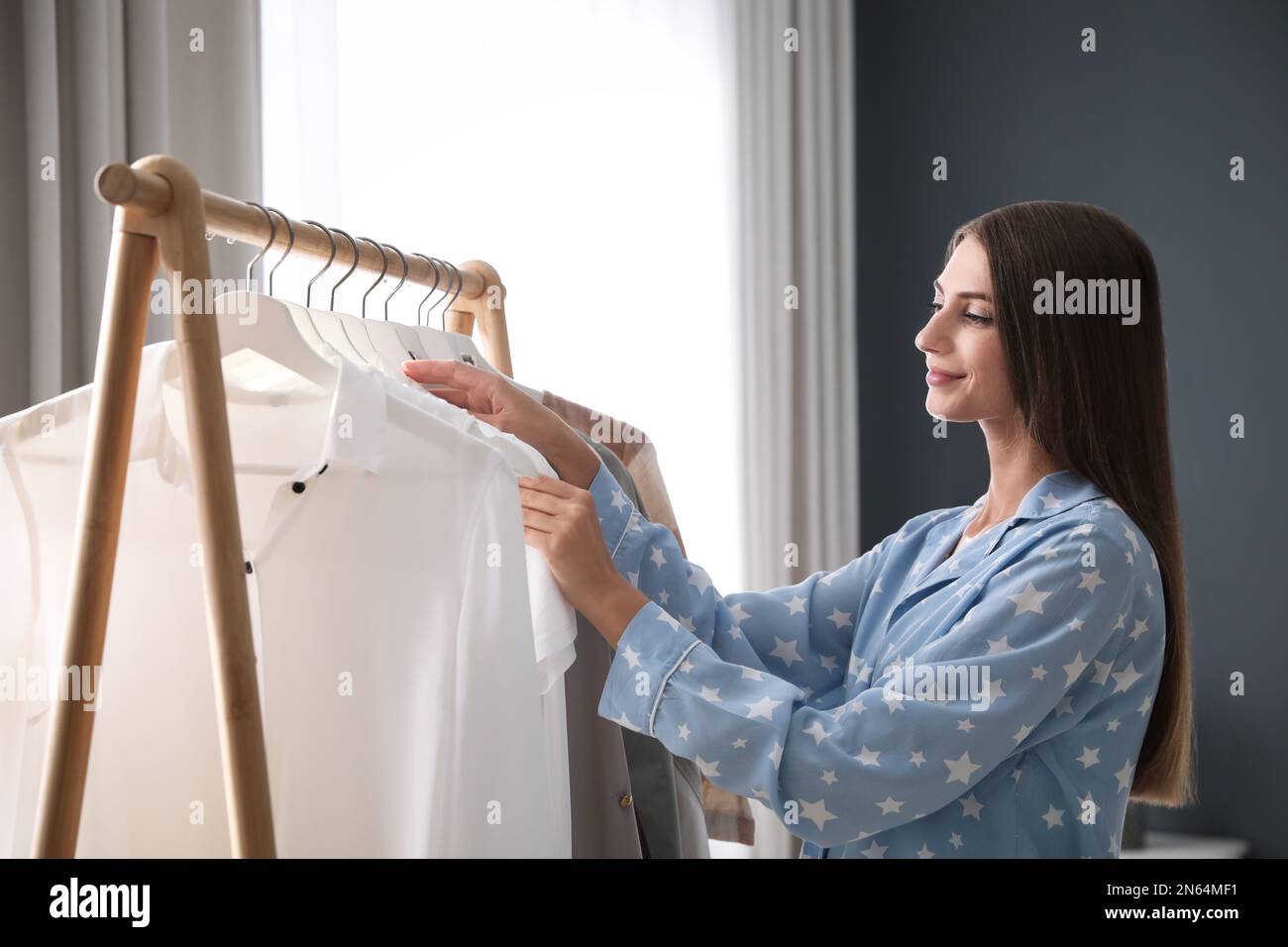 Woman taking shirt from rack with stylish clothes in room Stock Photo ...