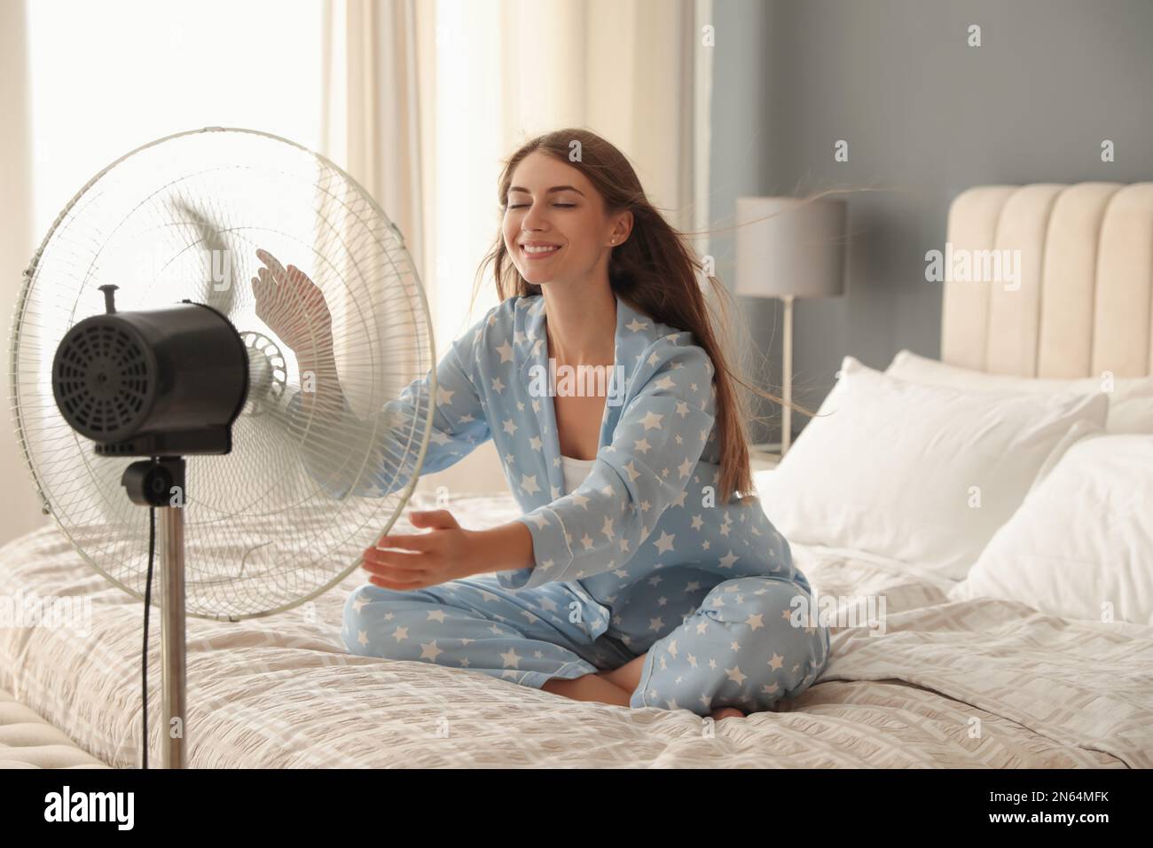 Woman enjoying air flow from fan on bed in room. Summer heat Stock ...