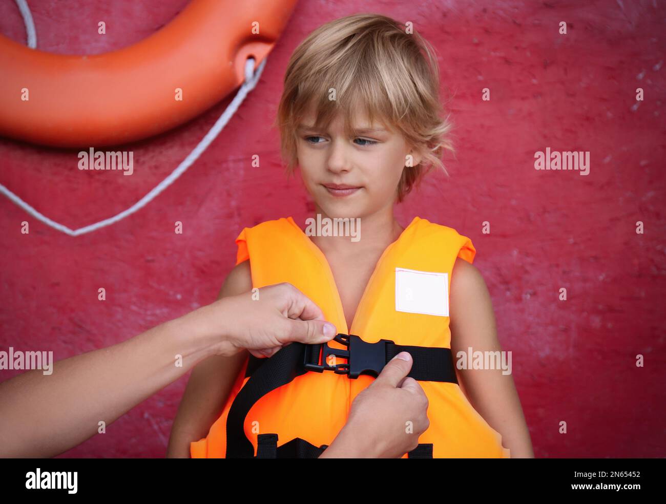 Rescuer putting orange life vest on child near red wall Stock Photo - Alamy