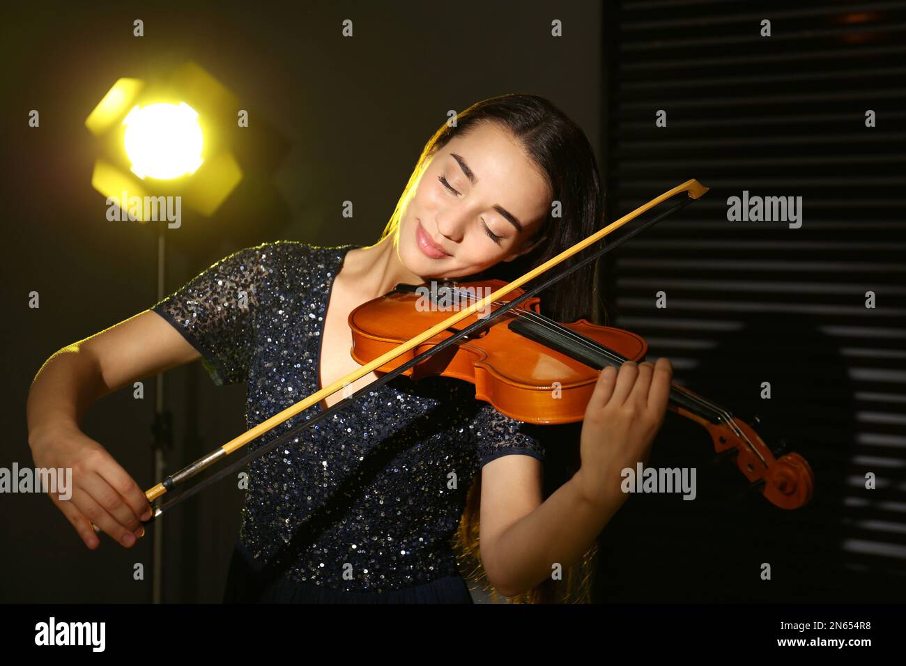 Beautiful young woman playing violin in dark room Stock Photo - Alamy