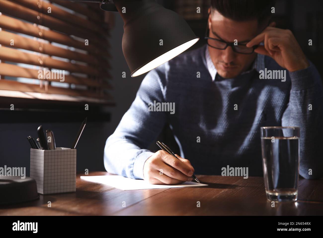 Man writing letter at wooden table in dark room, focus on hand Stock ...