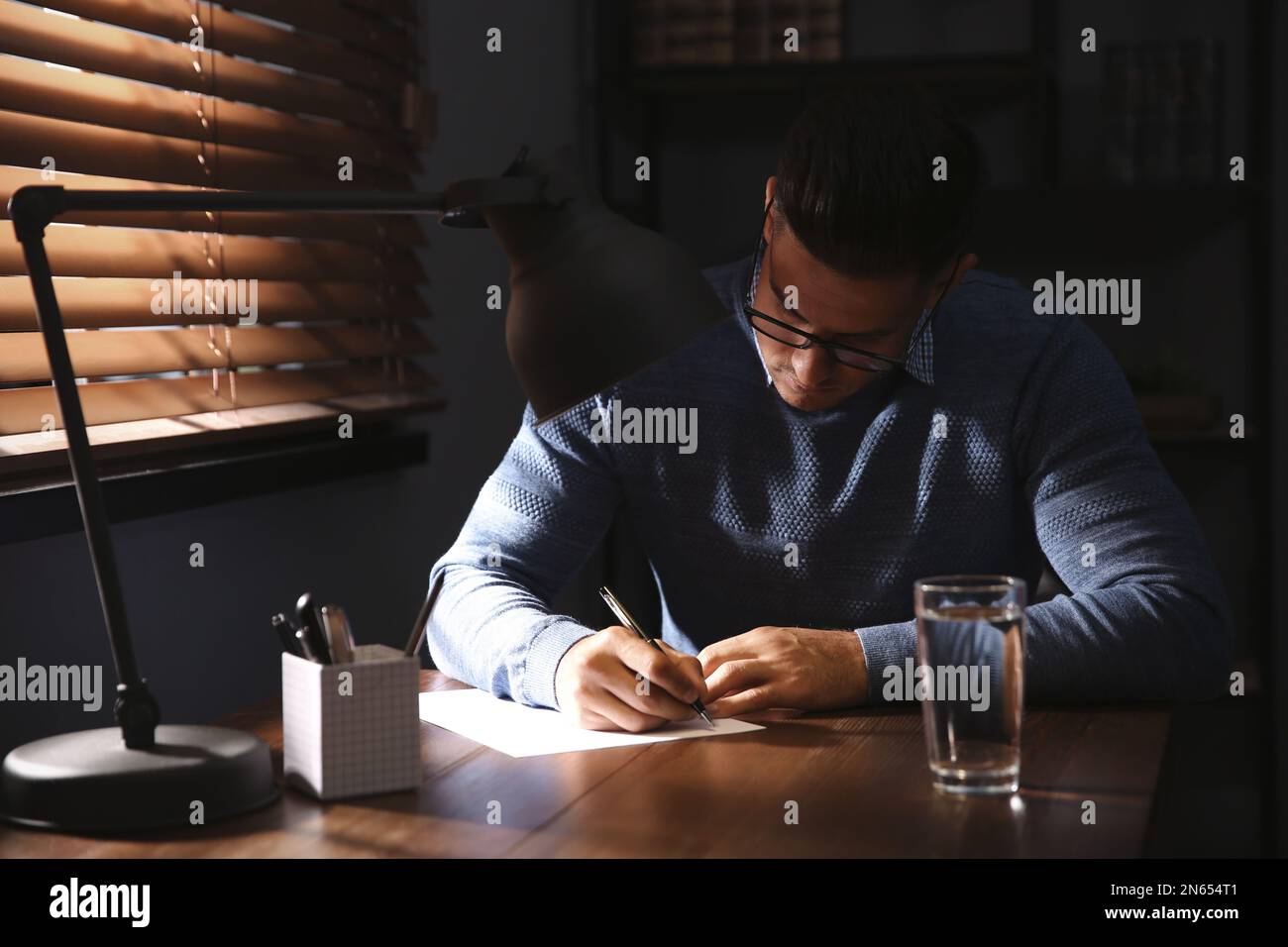 Man writing letter at wooden table in dark room Stock Photo - Alamy