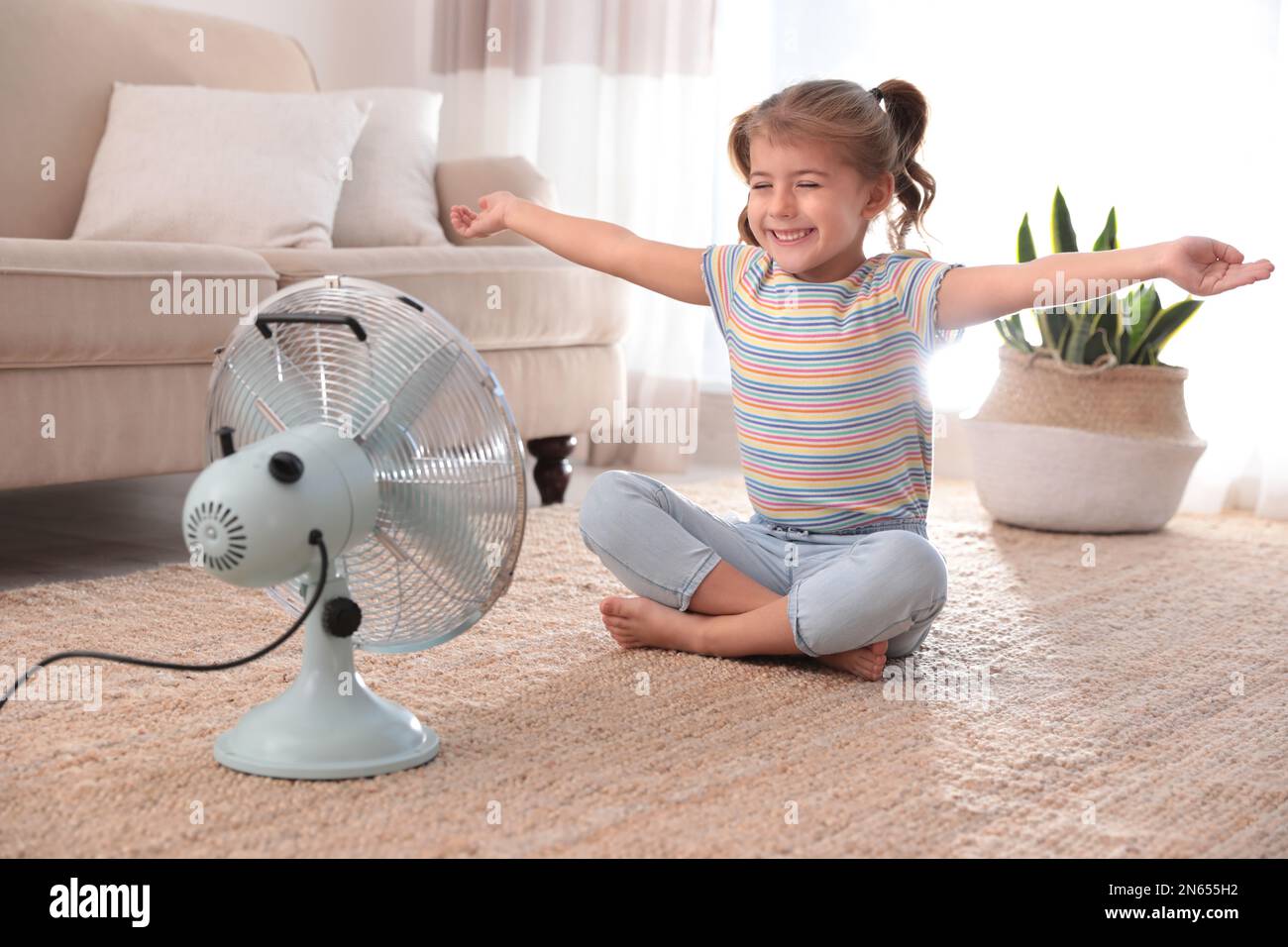 Little girl enjoying air flow from fan on floor in living room. Summer ...