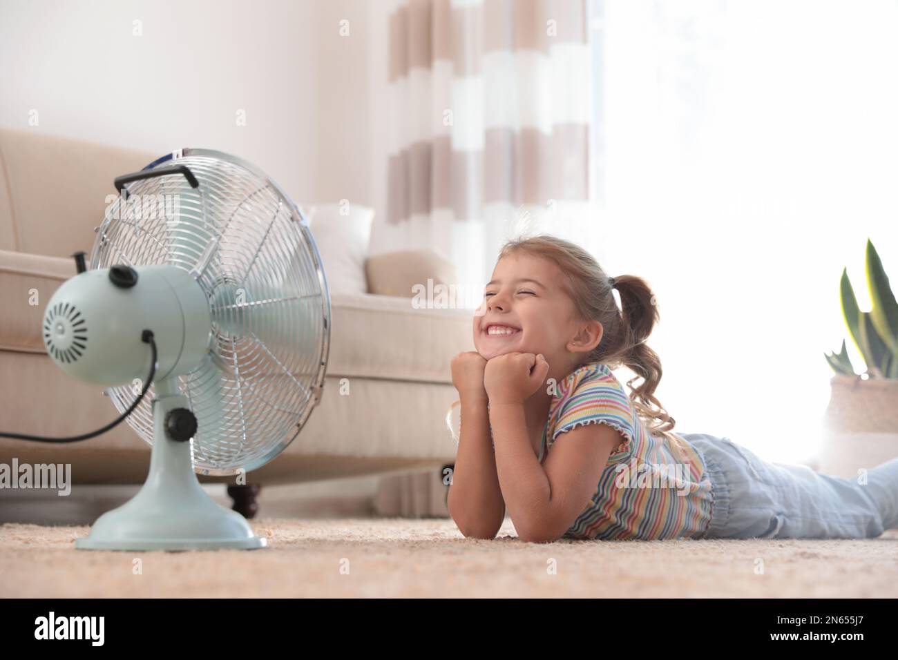 Little girl enjoying air flow from fan on floor in living room. Summer ...