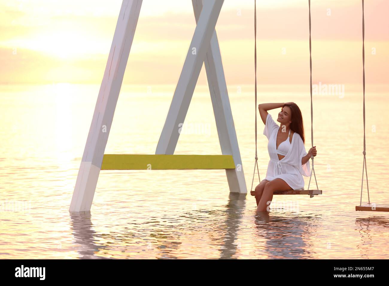 Young woman enjoying sunrise on swing over water Stock Photo - Alamy