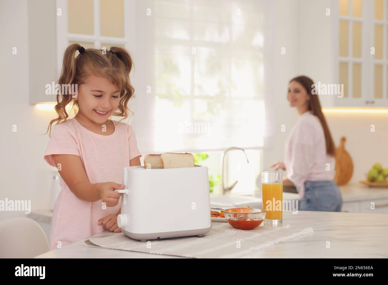 Cute little girl using toaster at table in kitchen Stock Photo - Alamy