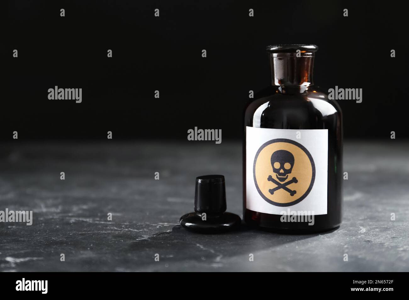 Open glass bottle of poison with warning sign on black table. Space for ...