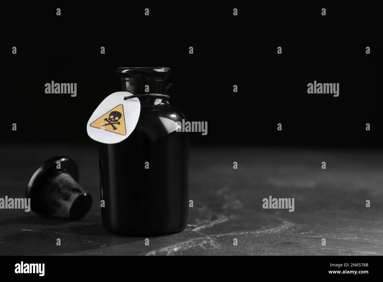 Open glass bottle of poison with warning sign on black table. Space for ...