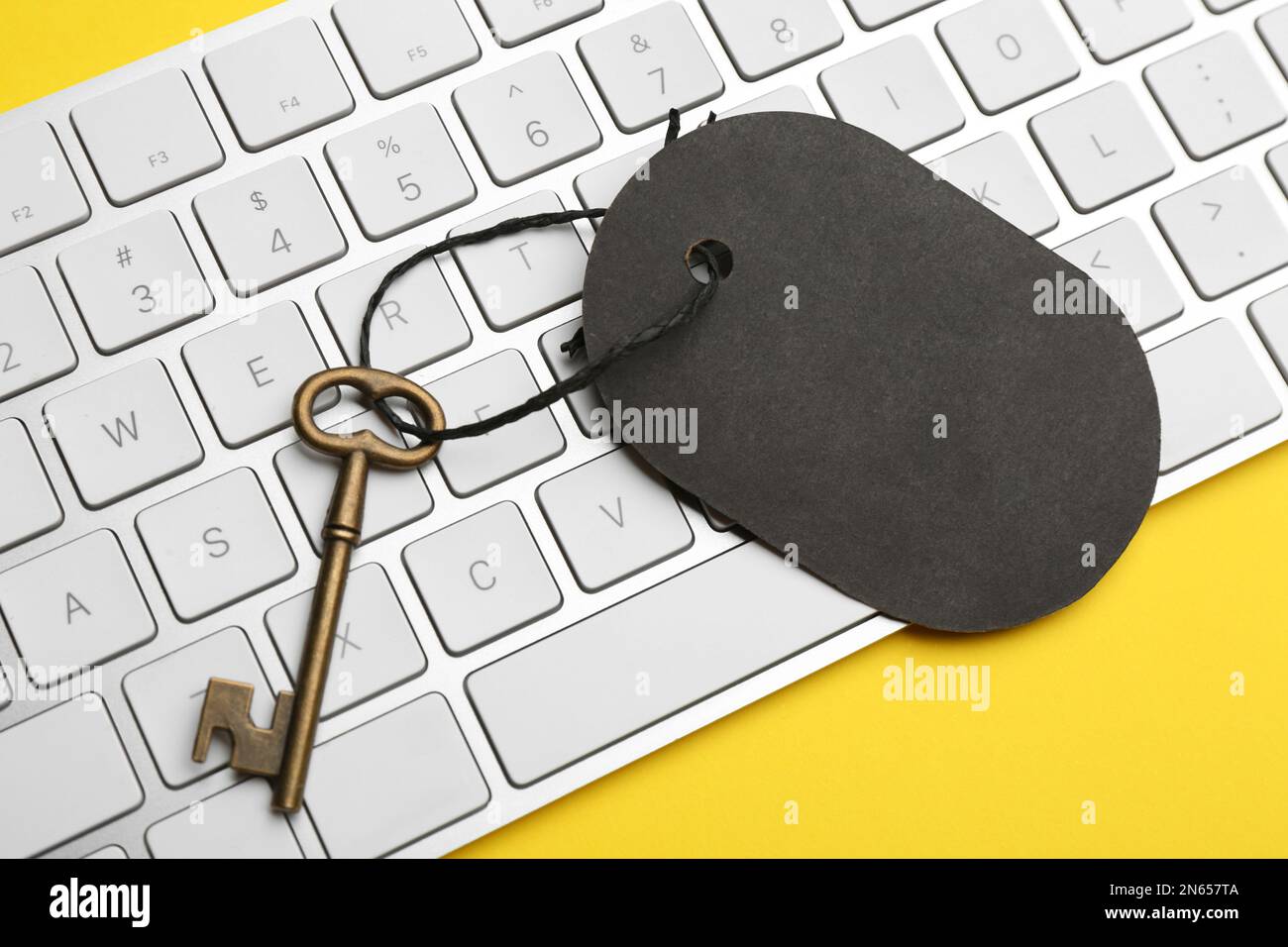 Vintage key with blank tag and keyboard on yellow background, closeup ...