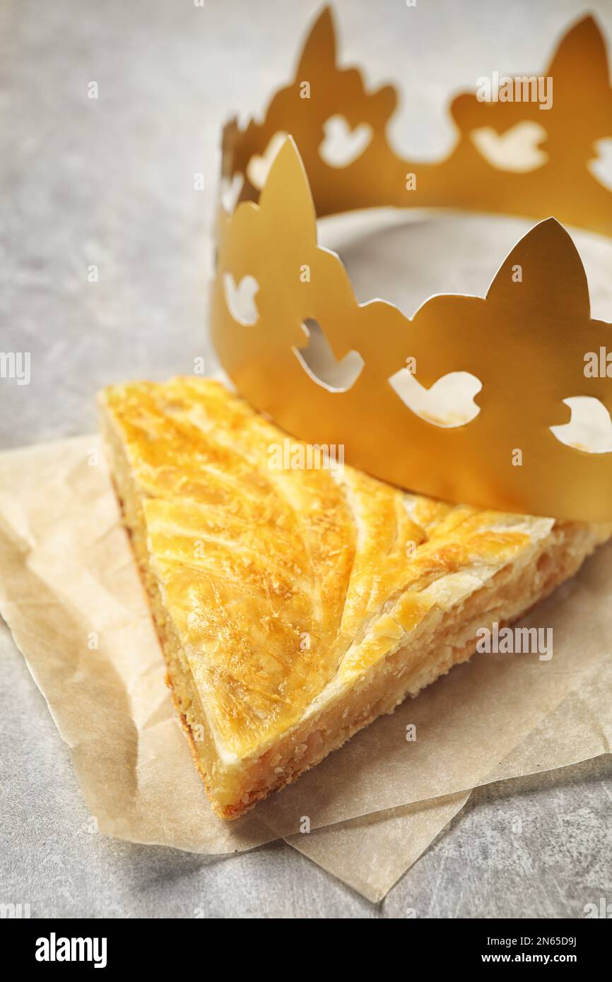 Slice of traditional galette des Rois with paper crown on light grey ...