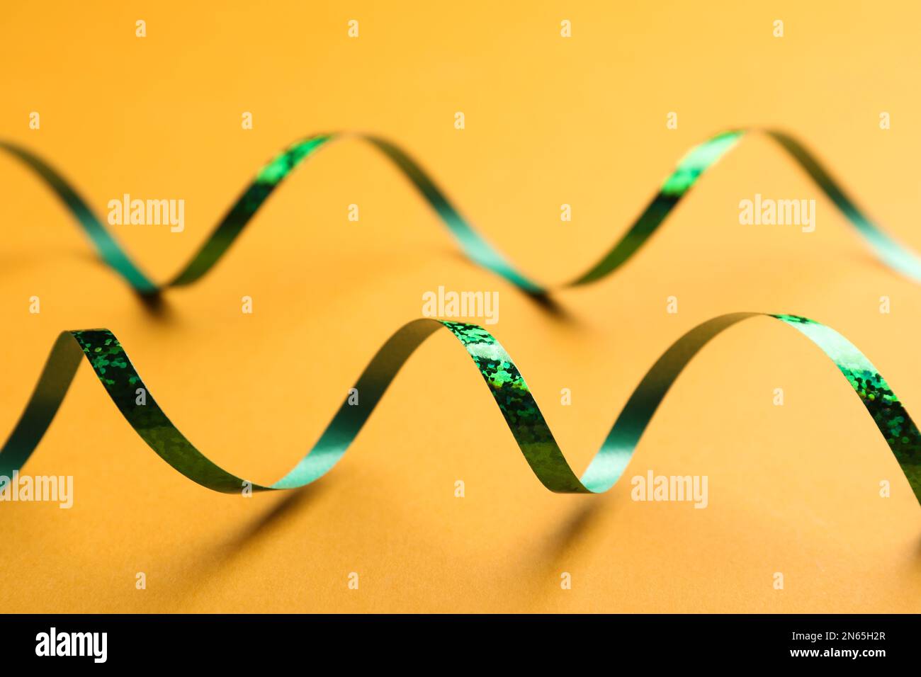Shiny green serpentine streamers on orange background, closeup Stock ...