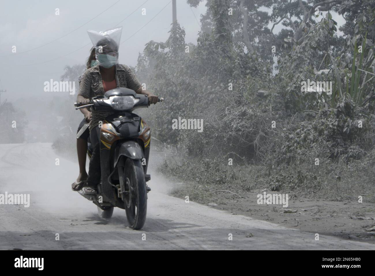 Villagers ride a motorcycle on a road covered with volcanic ash from ...