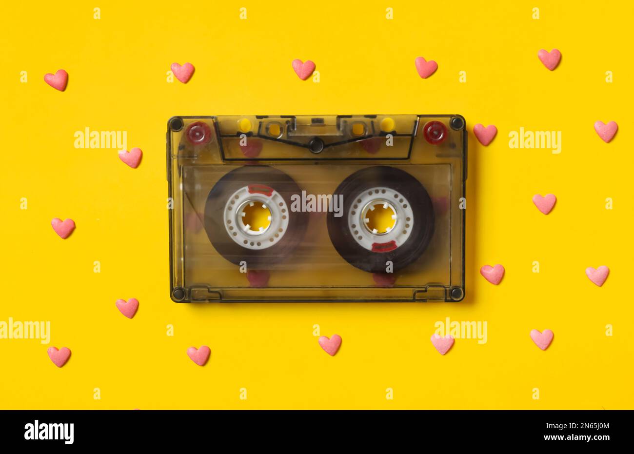 Music cassette and pink heart shaped sprinkles on yellow background ...