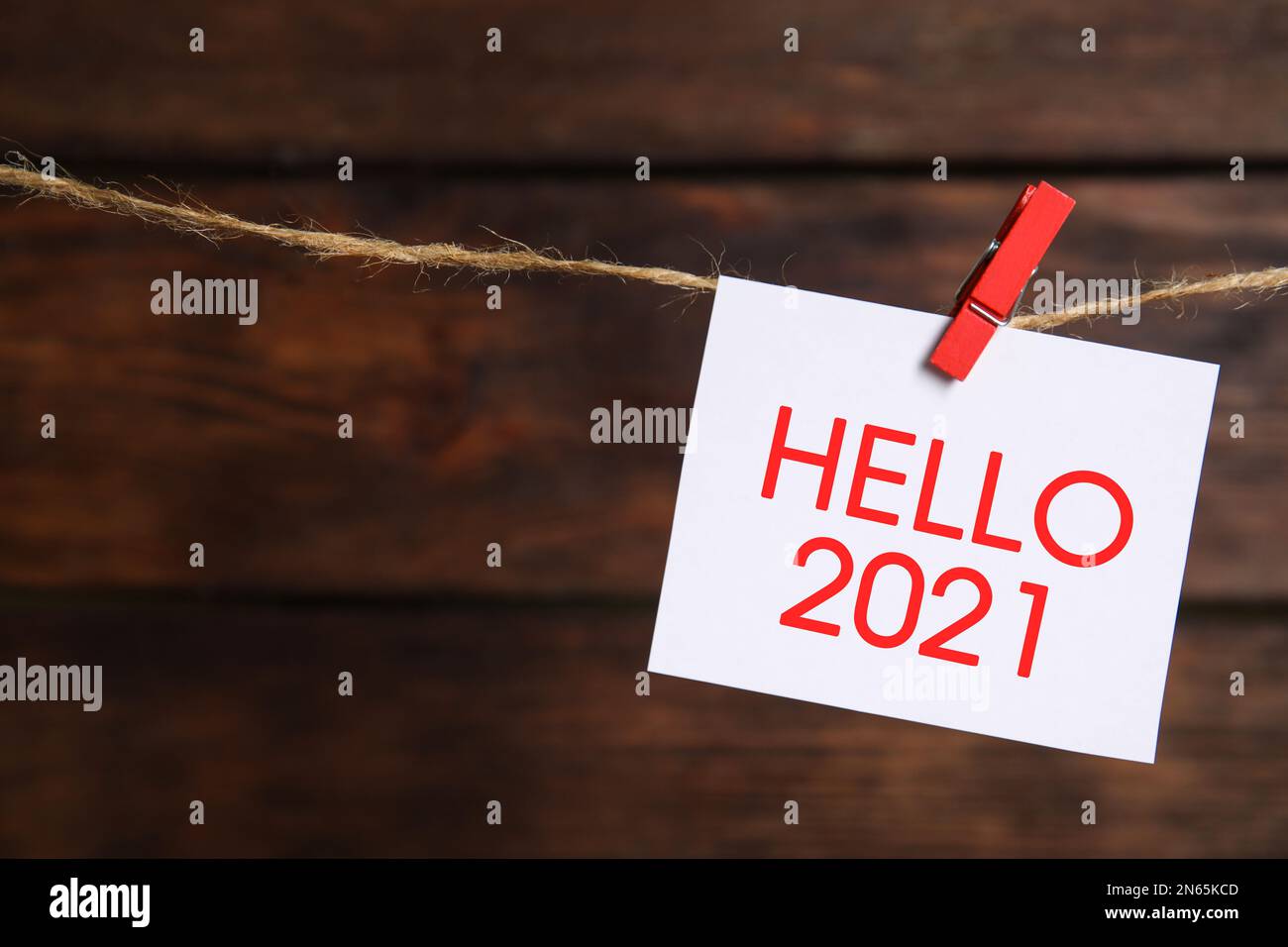 Paper note with phrase Hello 2021 hanging on twine against wooden ...