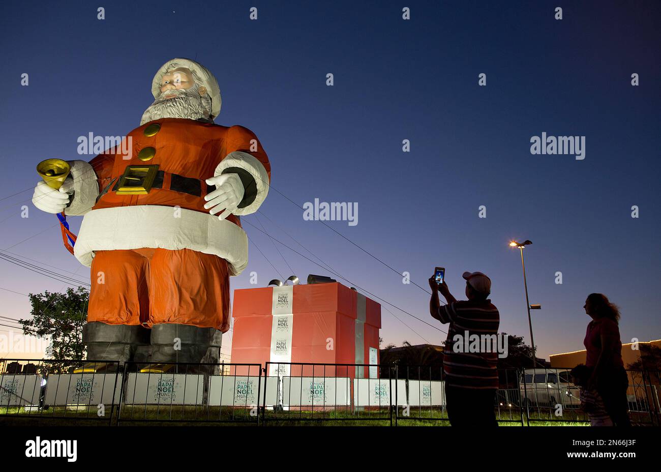 A man takes a picture of a giant Santa Claus statue that is on display ...