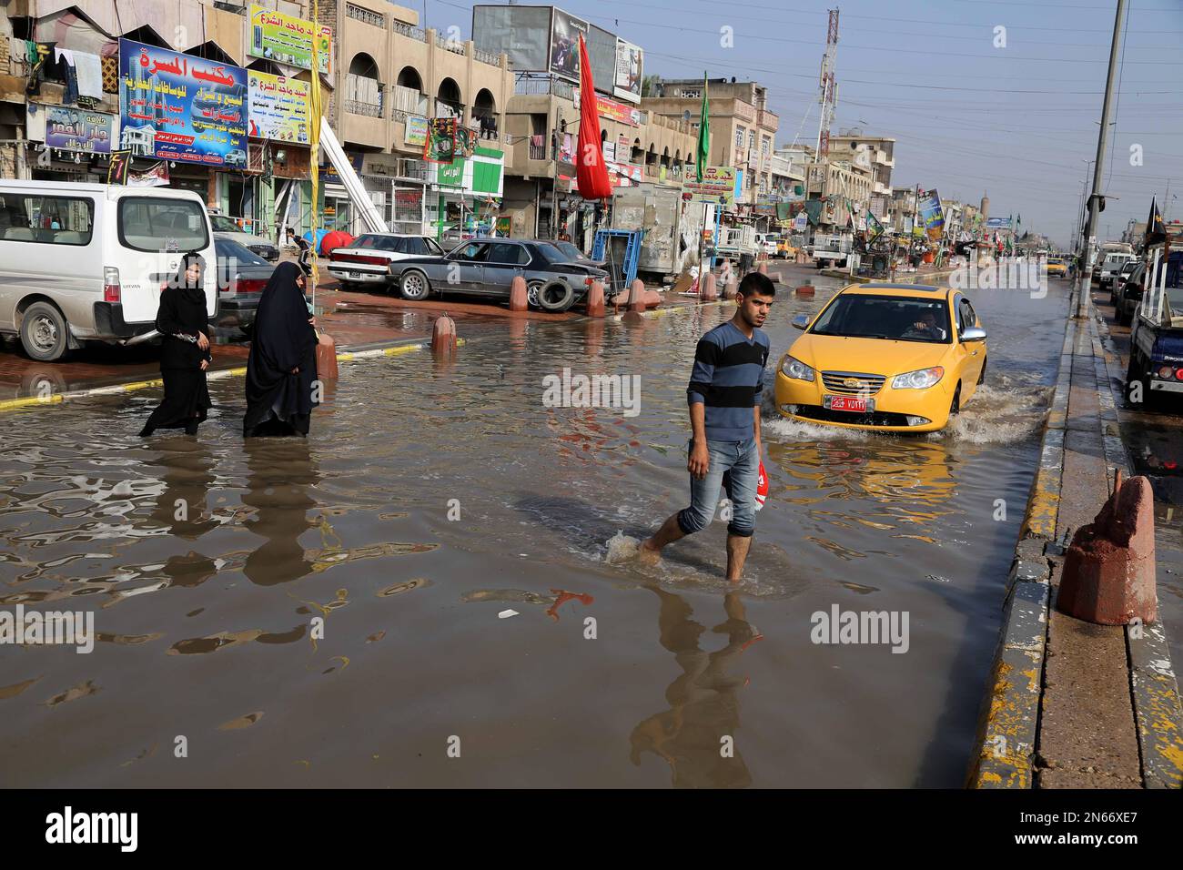Iraqis make their way through a flooded street after heavy rain fell in ...