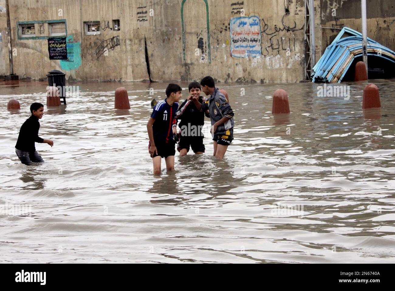 Iraqi boys make their way through a flooded street after heavy rain ...