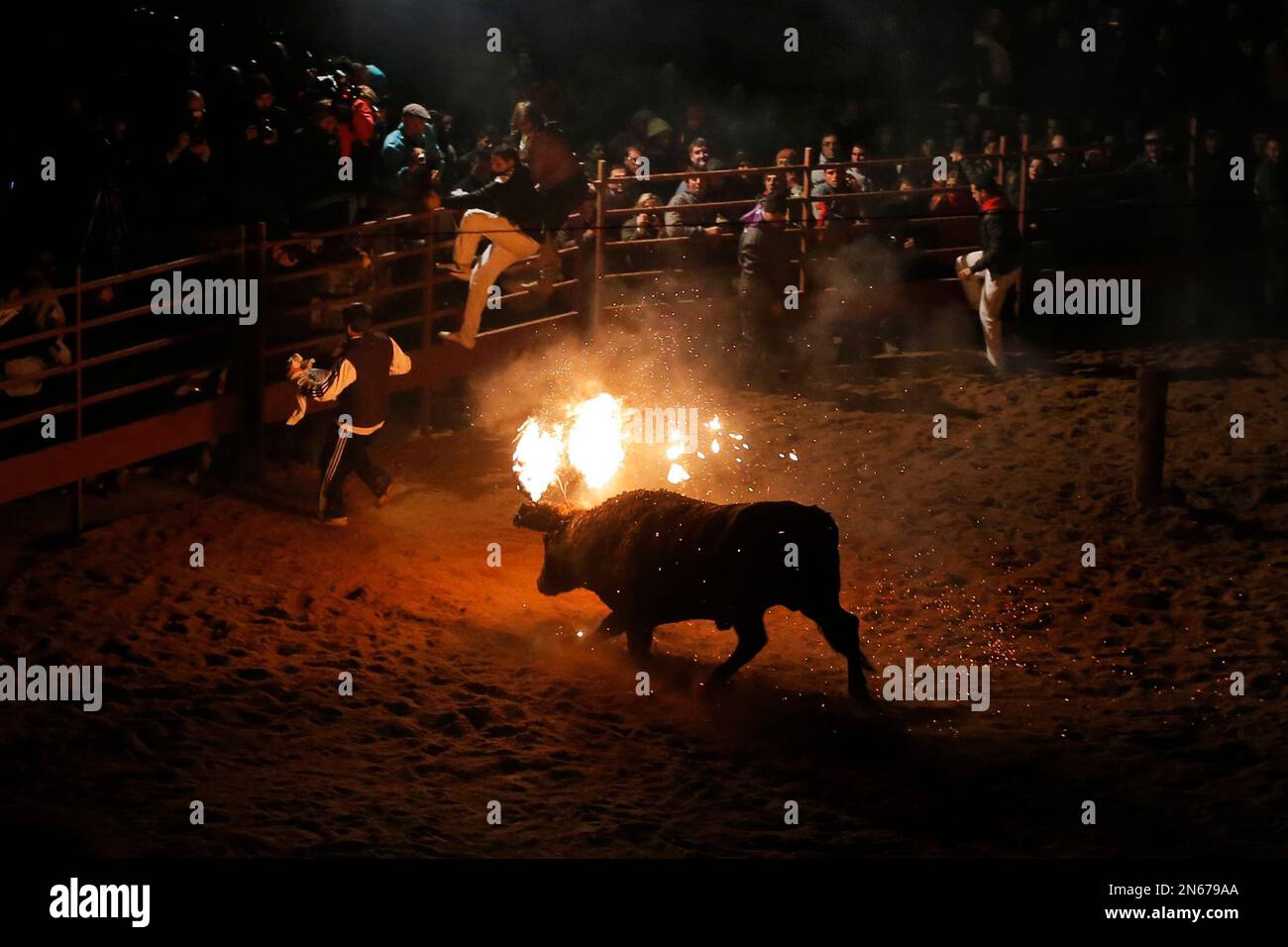 Revelers jump over the barricades as a fire bull chases them during the ...