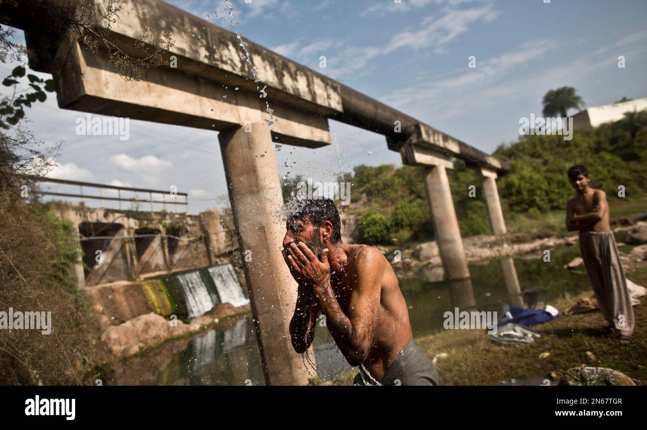 A Pakistani worker takes a shower under a leaking water supply pipe ...