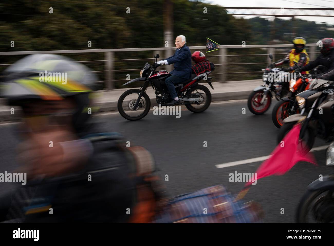 A biker wearing a mask depicting President Joe Biden rides in the ...