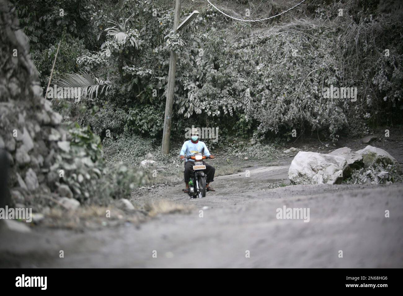 A man wearing a mask rides on his motorbike through a road covered with ...