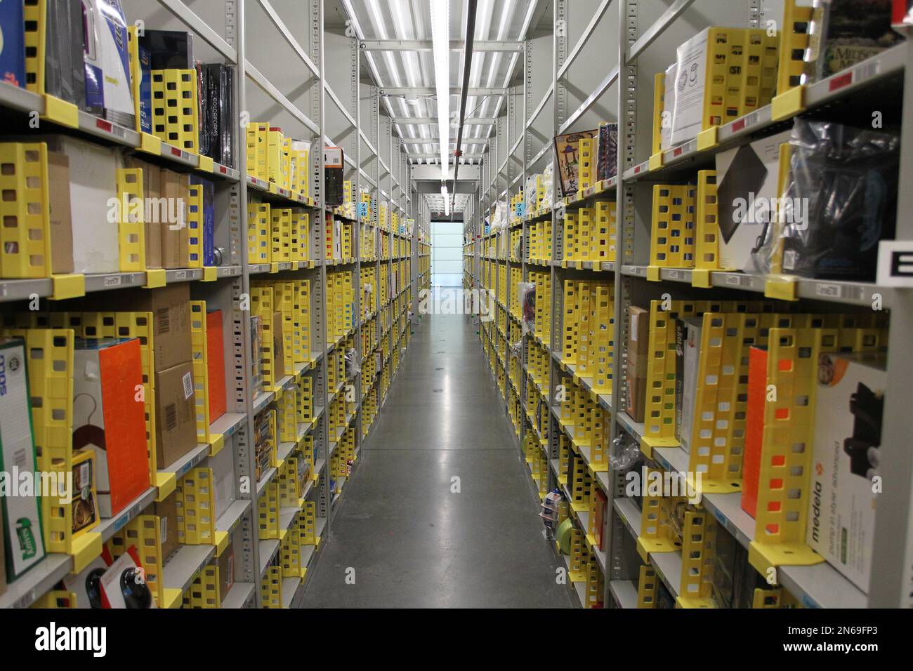 Aisles of shelves hold products to be shipped at the Amazon San ...