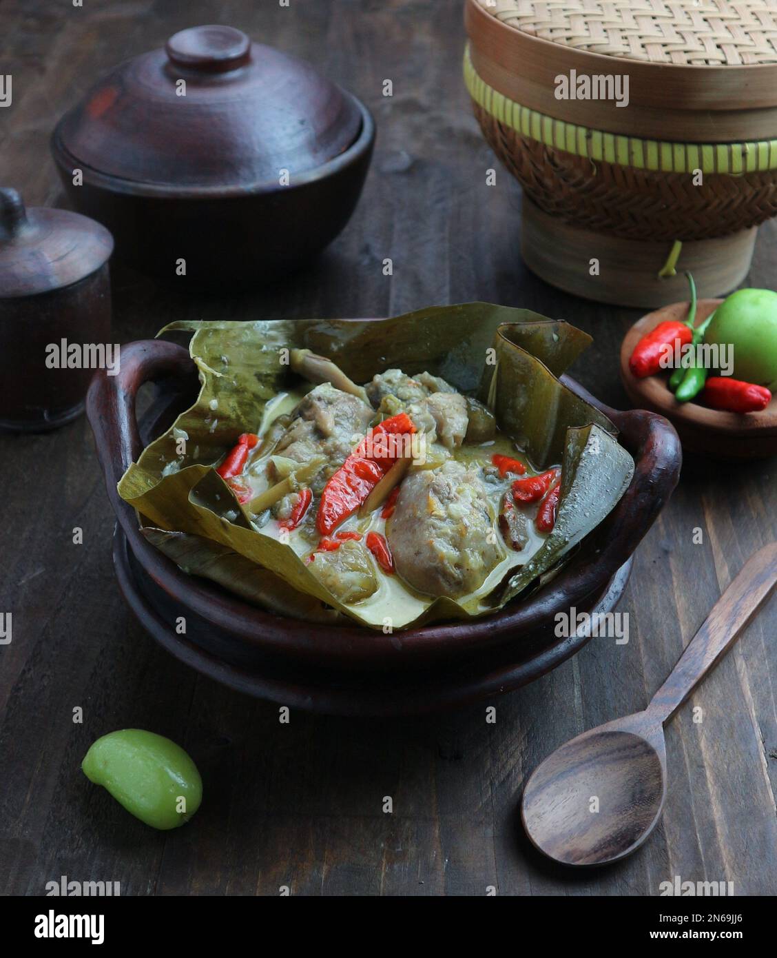 Spicy and sour steamed chicken in banana leaves served on a clay plate ...