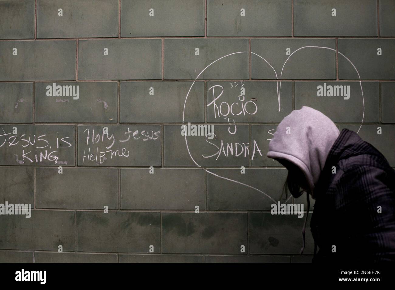 A homeless woman walks past graffiti on a wall outside a shelter in the ...