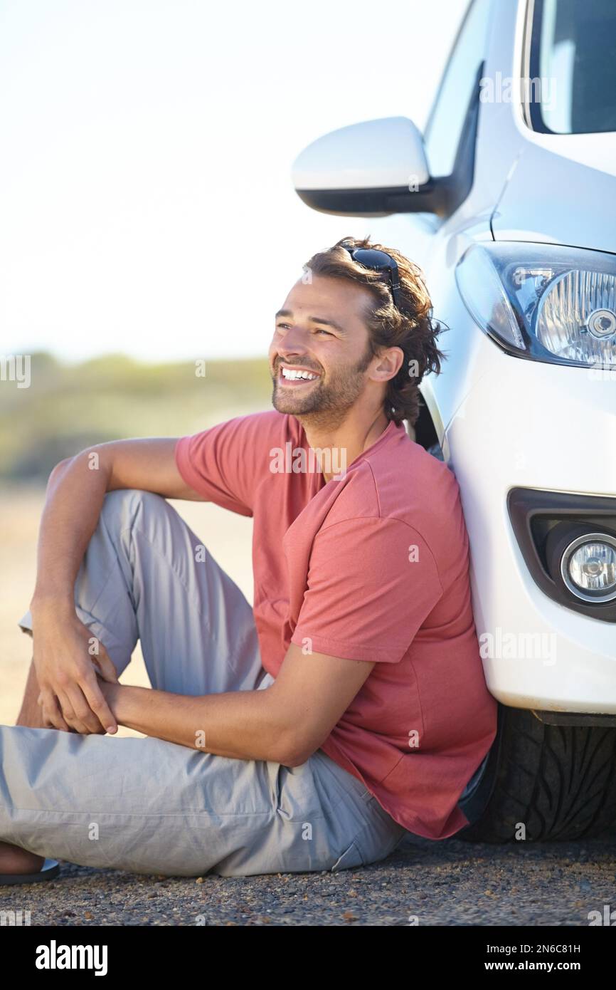 Taking a break from driving. A young man sitting on the road against ...