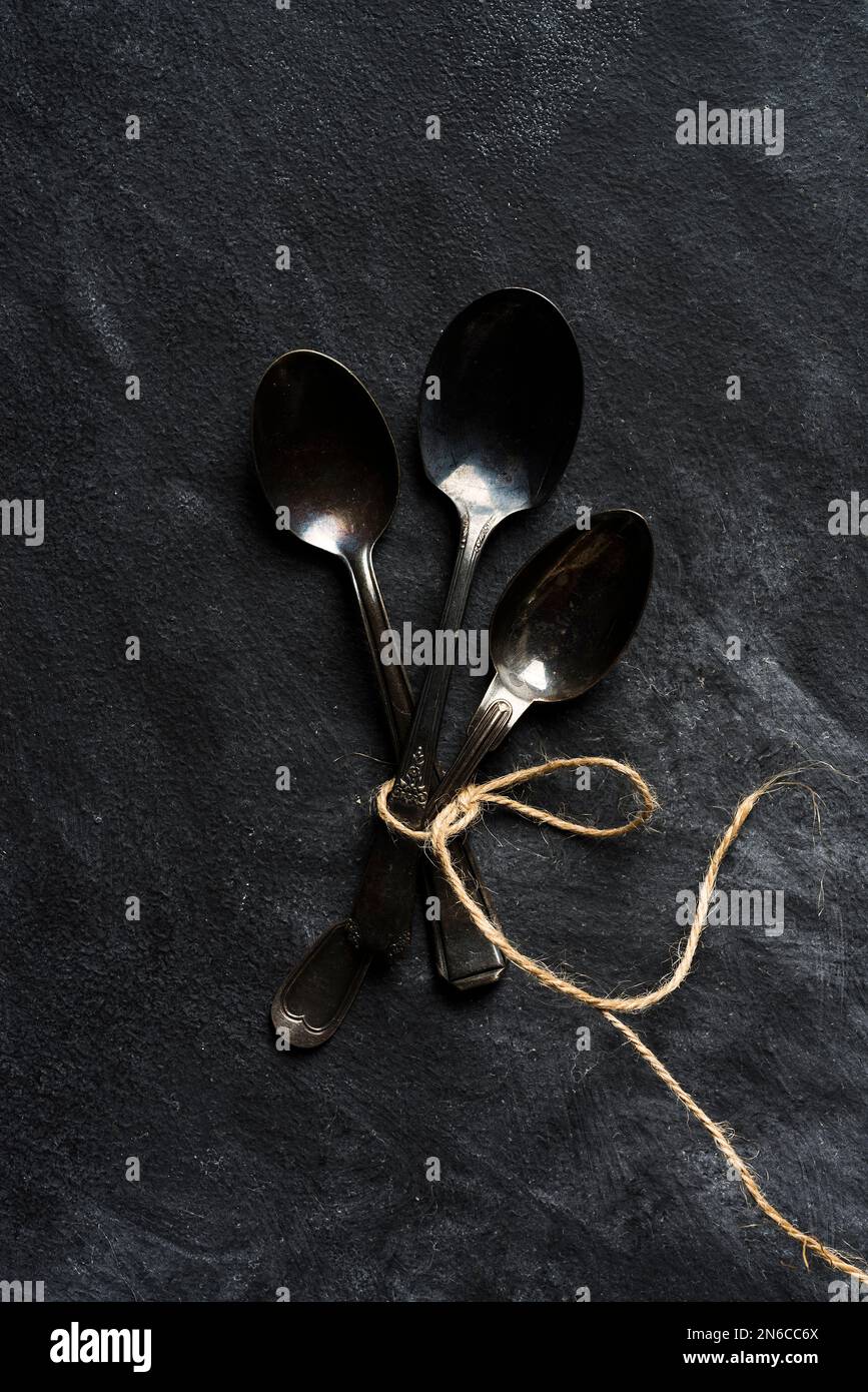 Three vintage silver spoons tied with jute string on black background ...