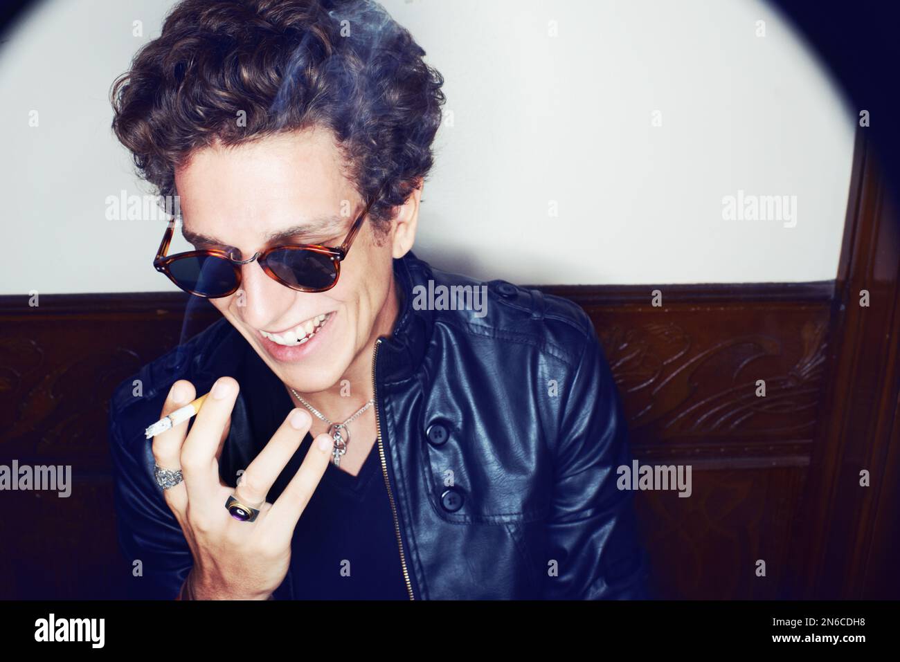 Casual smoker. A young man sitting in a hallway laughing while enjoying ...