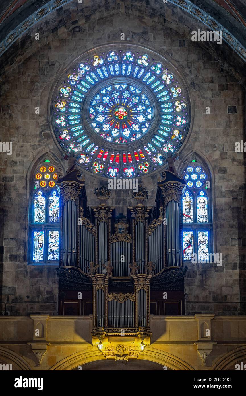 A nice musical organ with a large stained glass window behind colors ...