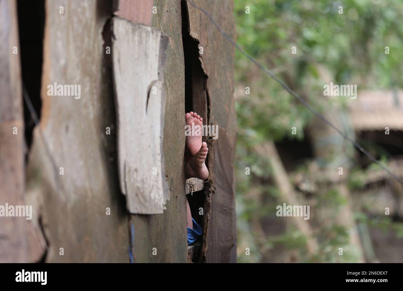 A Filipino boy rests his foot on the damaged wall of his house that was ...