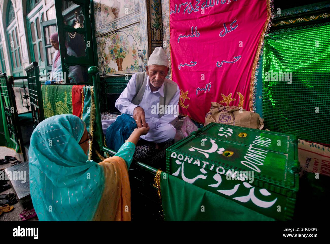 A Kashmiri Muslim woman receives sweets from a priest at the shrine of ...