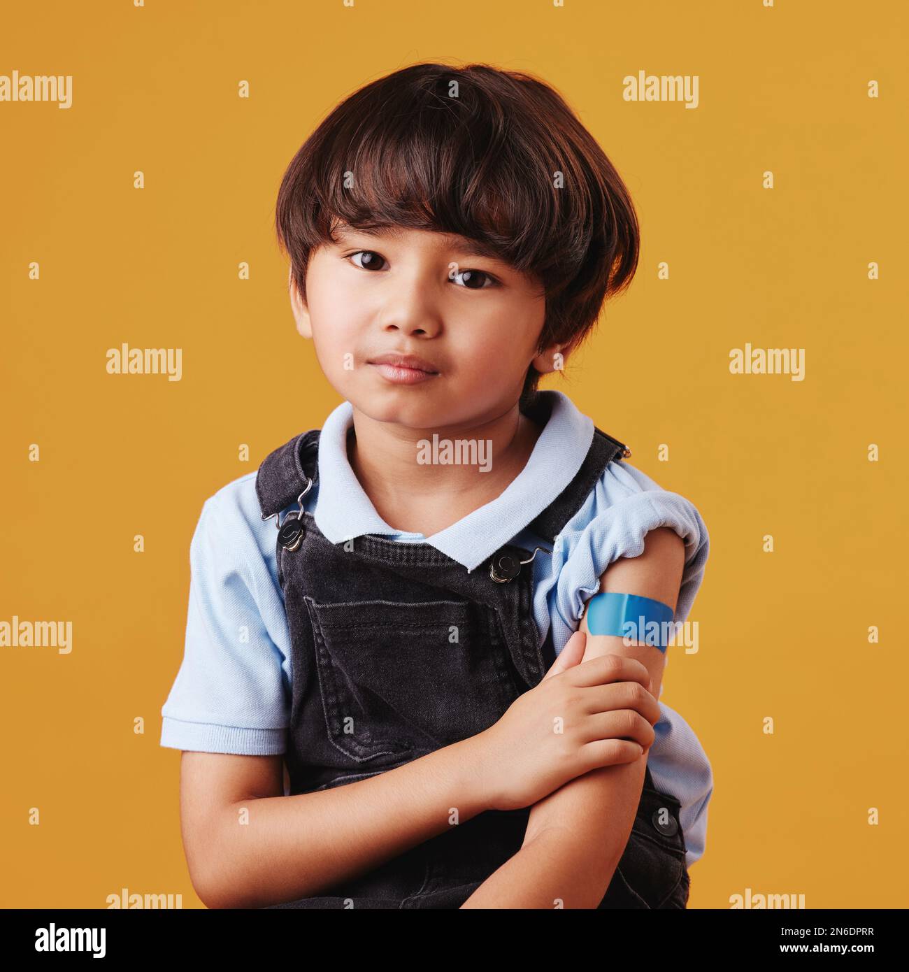 Portrait of a little asian boy holding his arm and showing his bandaid ...