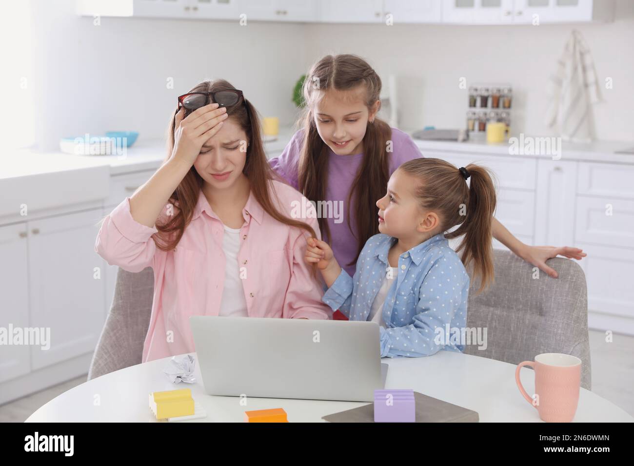 Children disturbing stressed woman in kitchen. Working from home during ...