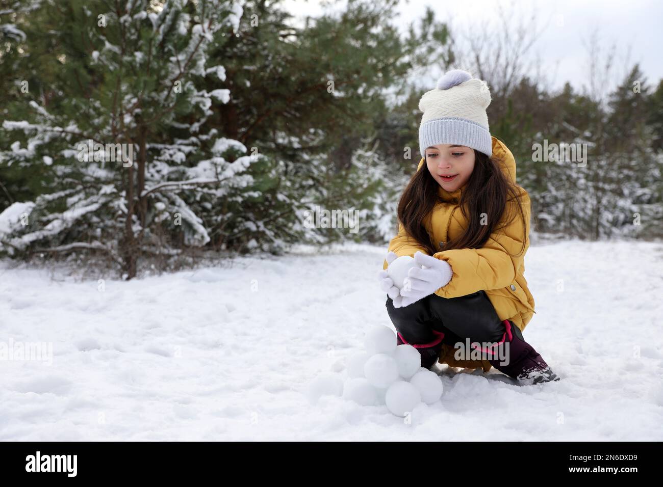 Cute little girl rolling snowballs in winter forest Stock Photo - Alamy