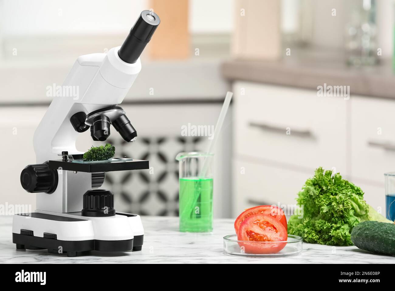 Microscope and fresh vegetables on table in laboratory, space for text ...