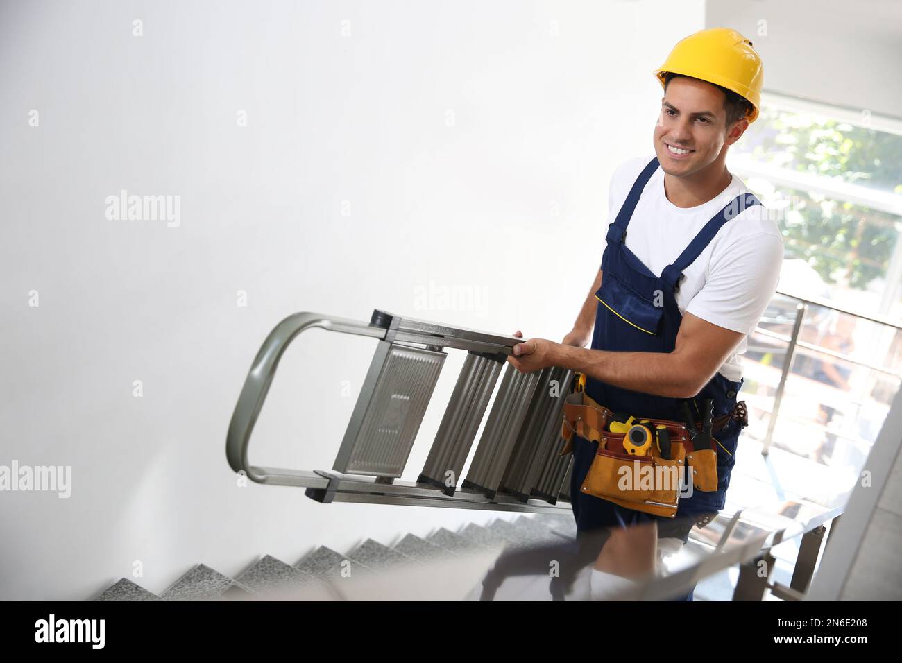 Professional builder carrying metal ladder up stairs Stock Photo - Alamy