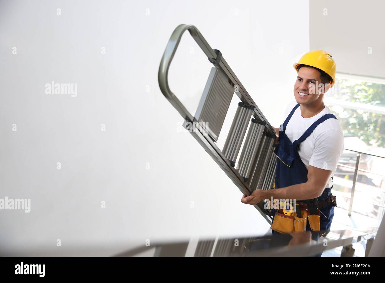 Professional builder carrying metal ladder up stairs Stock Photo - Alamy